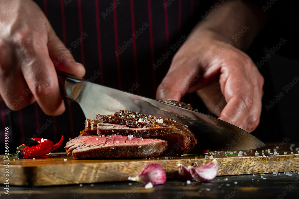 Chef hands slicing beef steak with knife on wood cutting desk. Top view ...