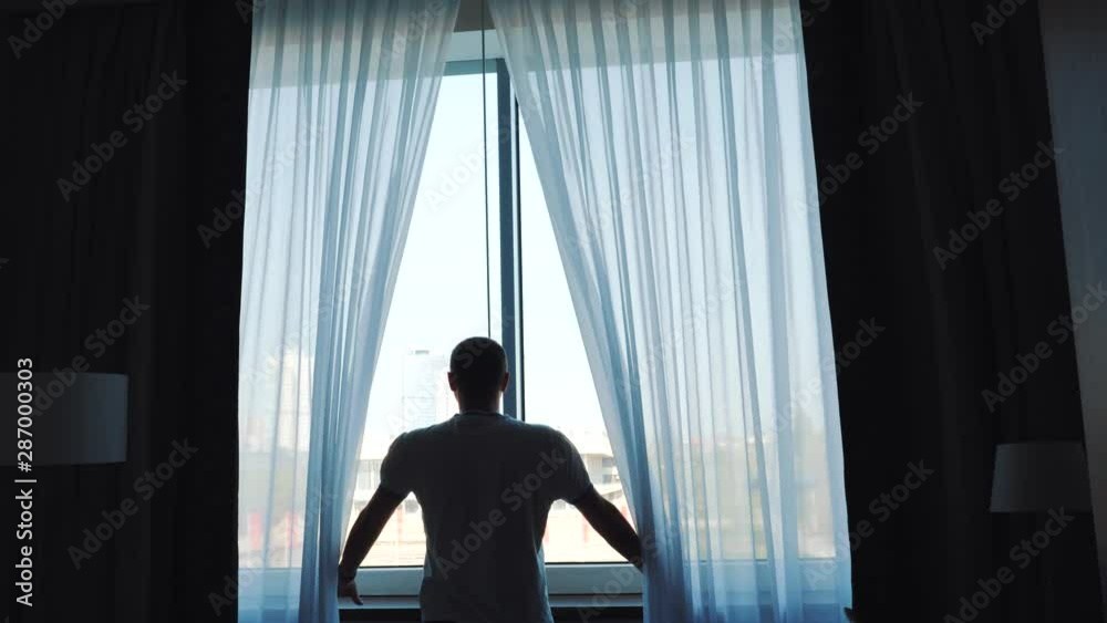 A young man comes to the window of the room, office, hotel, opens the ...