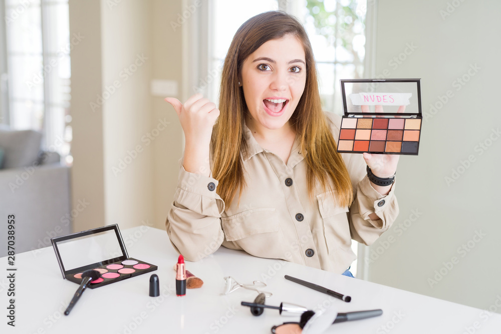 Beautiful young woman using make up cosmetics applying color from palete pointing and showing ...