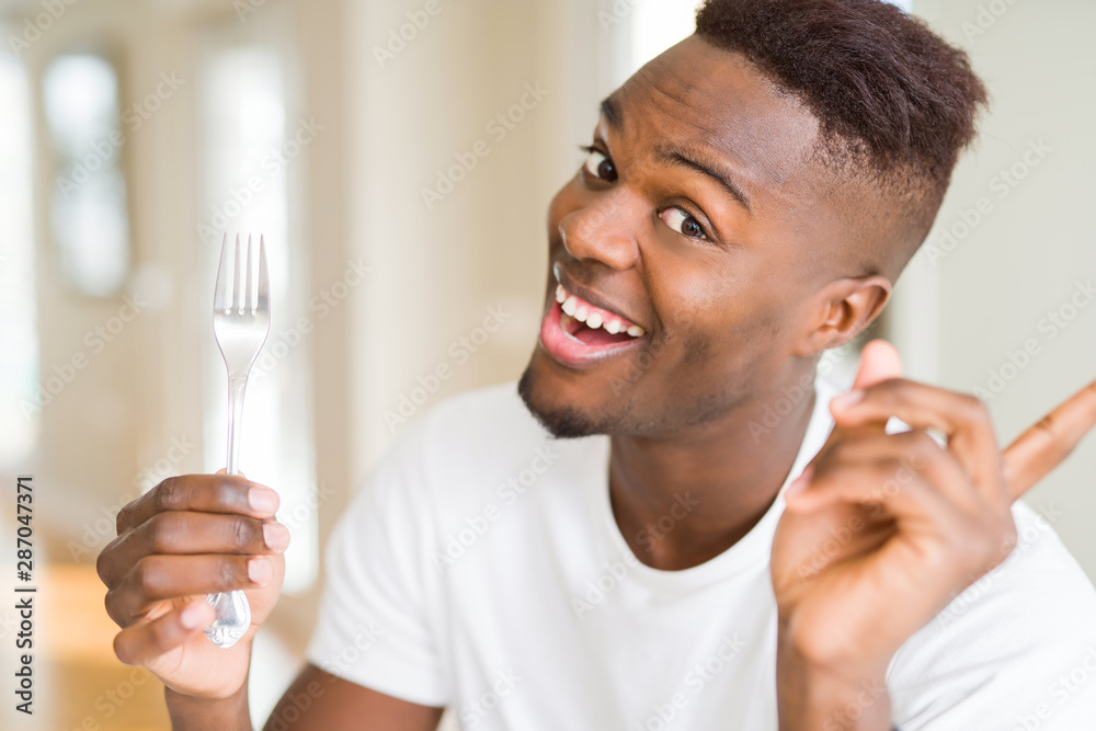 African american man holding silver fork cutlery very happy pointing ...