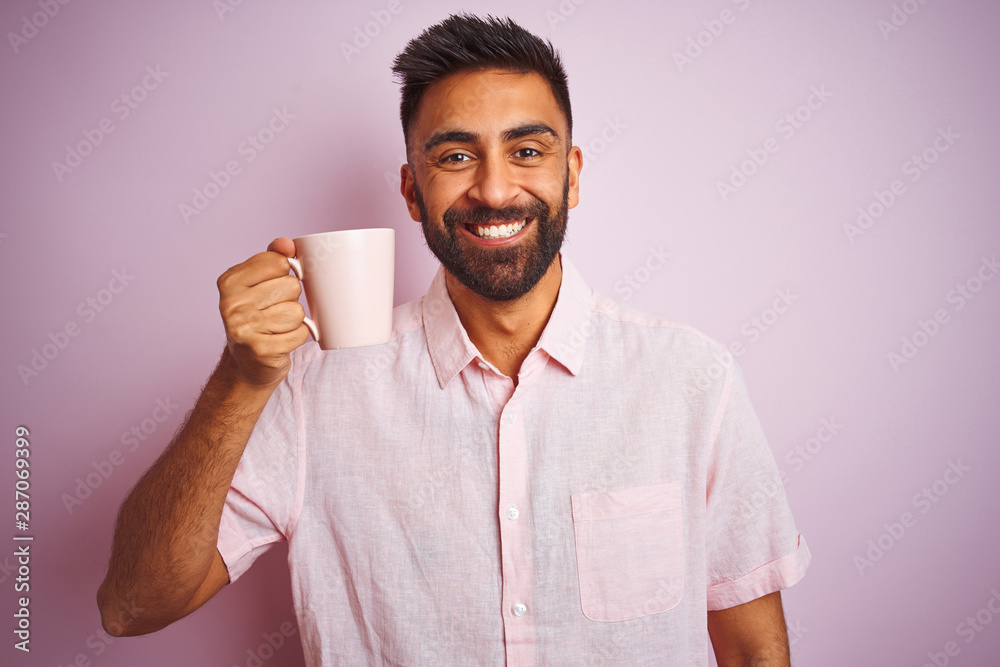 Young indian man wearing shirt drinking cup of coffee standing over ...
