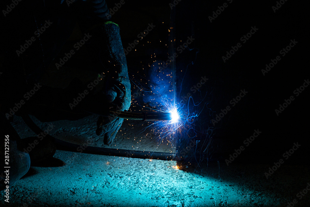 Blue flame and sparks flying around factory floor from welding machine ...