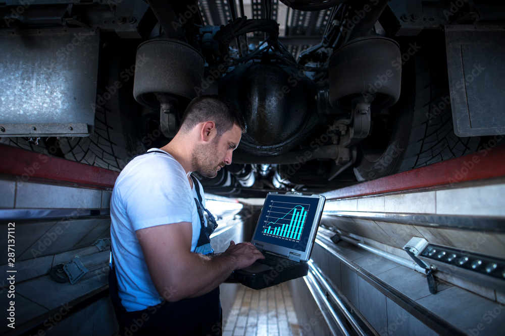 Vehicle mechanic with diagnostic tool laptop working under the truck in ...