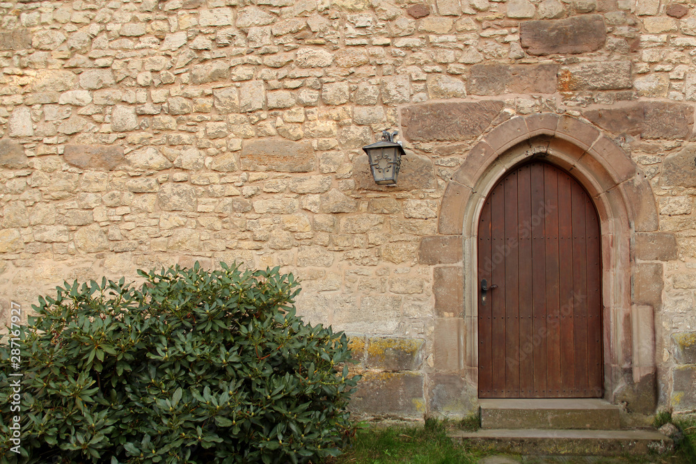 rough sandy old medieval stone wall with arched door and wrought iron ...