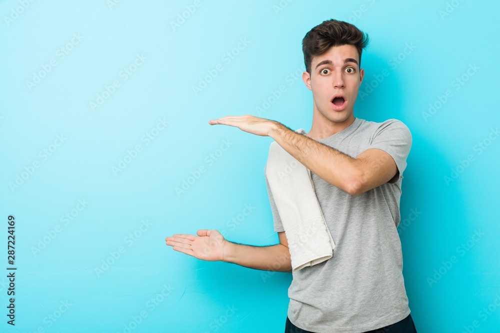 Young fitness teenager man shocked and amazed holding a copy space ...