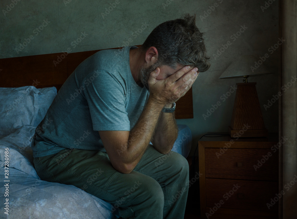 Attractive depressed and sad man at home sitting on bed crying ...