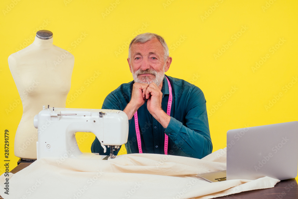 pleasing old man working in tailoring studio making clothes at sewing ...