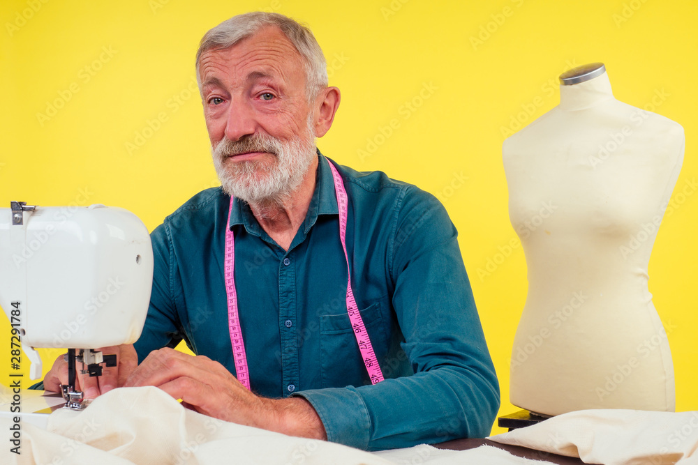 pleasing old man working in tailoring studio making clothes at sewing ...