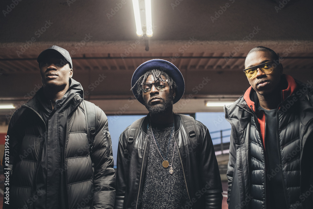portrait three young black men posing in a parking lot looking away ...