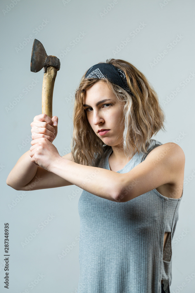 The girl is furious with an ax, studio photo on a gray background. The ...