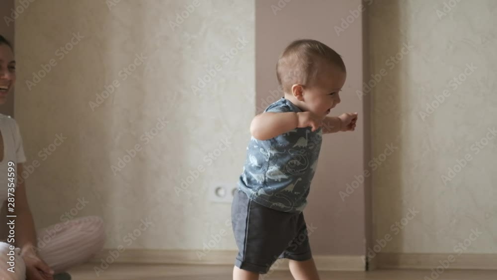 Cute baby doing the first steps and falls in slow motion at home near ...