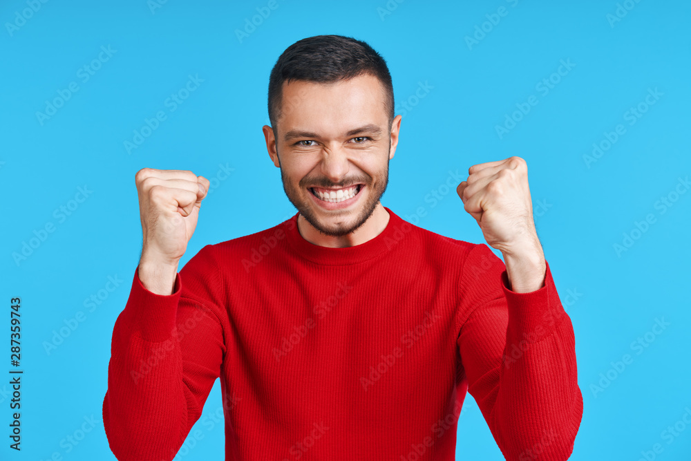 Happy man celebrating his success with winner gesture on blue ...