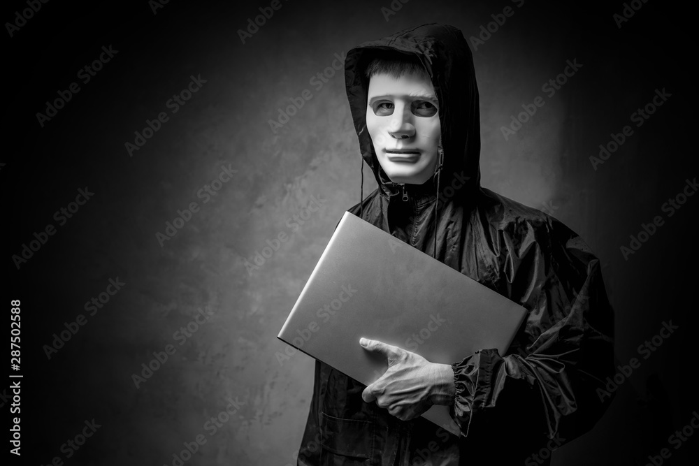 Anonymous hacker in white mask holding a laptop in the dark. Data thief ...