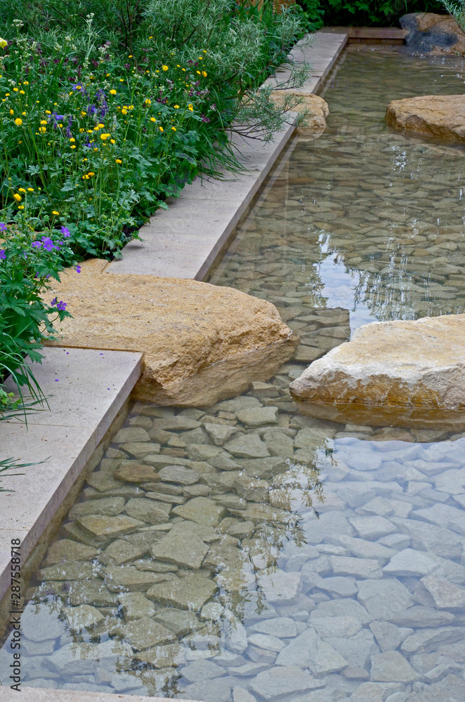 Modern water garden with flowing rill with rocks, stepping stones and ...