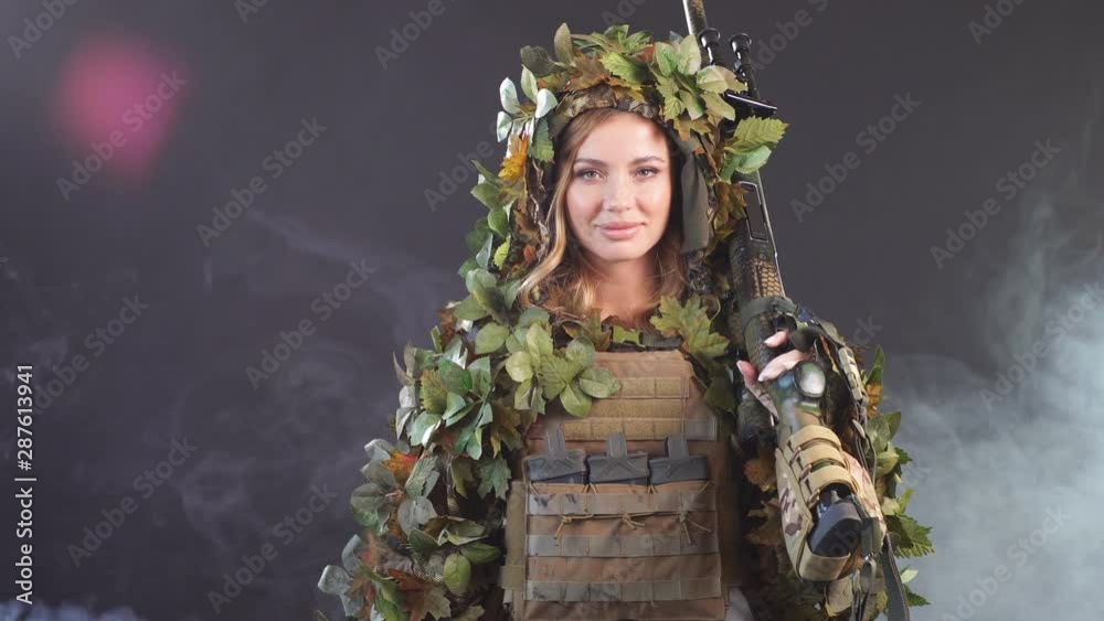 Camouflaged woman sniper in ghillie suit posing with rifle in foggy night. Special Weapons and ...