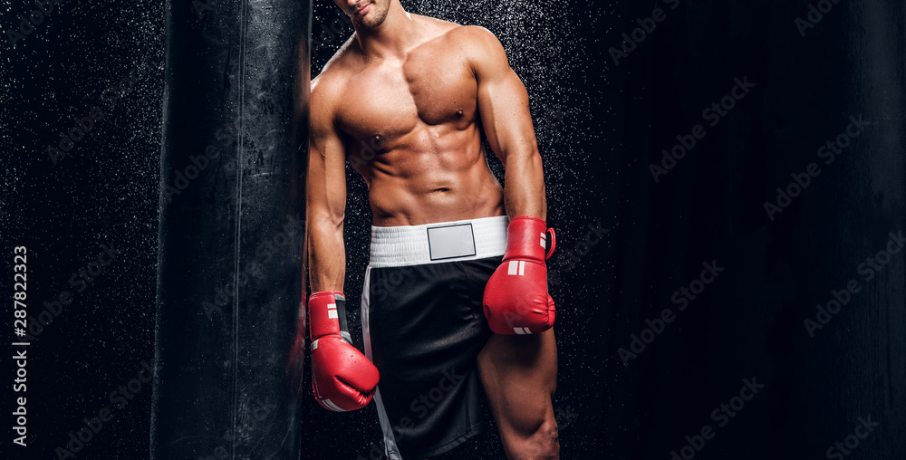 Young sexy fighter with nacked torso is posing in dark room near black ...