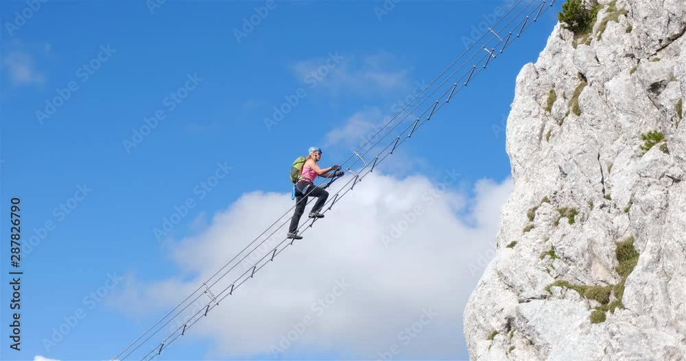 Woman moving high on a via ferrata diagonal ladder on Donnerkogel ...