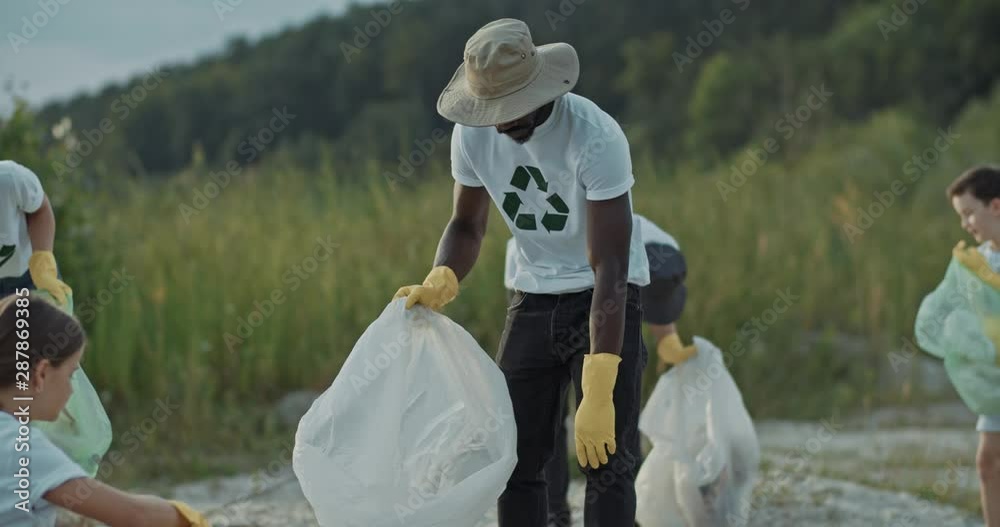 Helpful african guy picking up plastic garbage on sandy beach cleaning ...