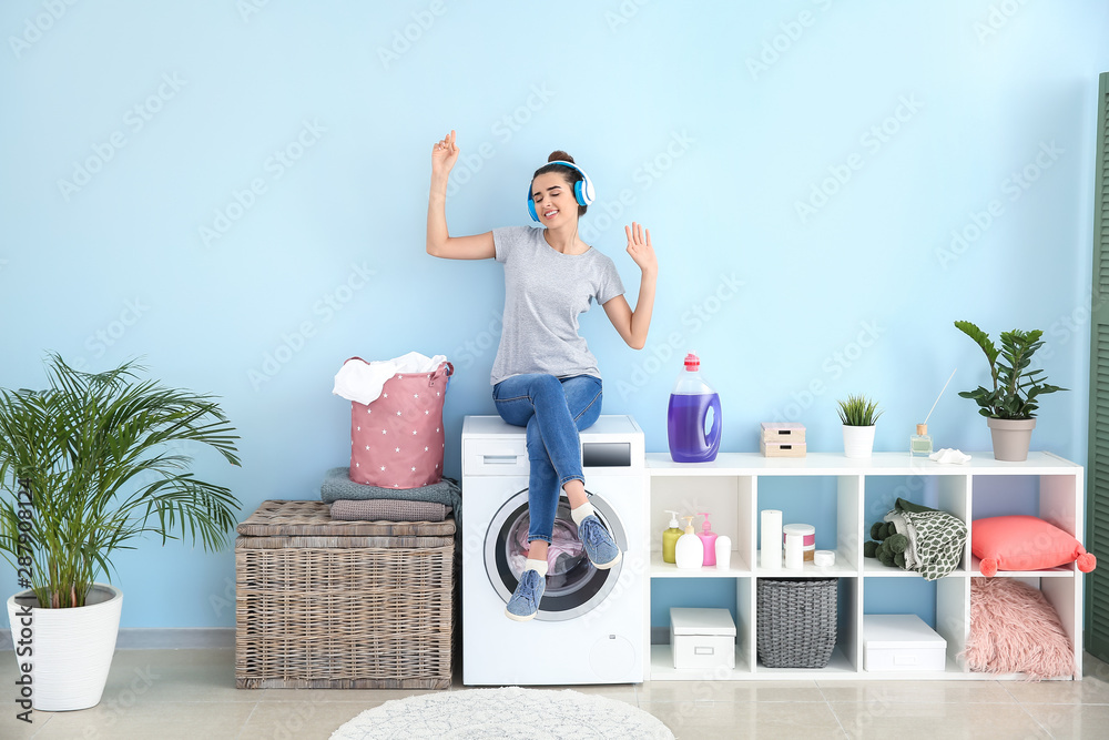 Beautiful young woman listening to music while doing laundry at home ...