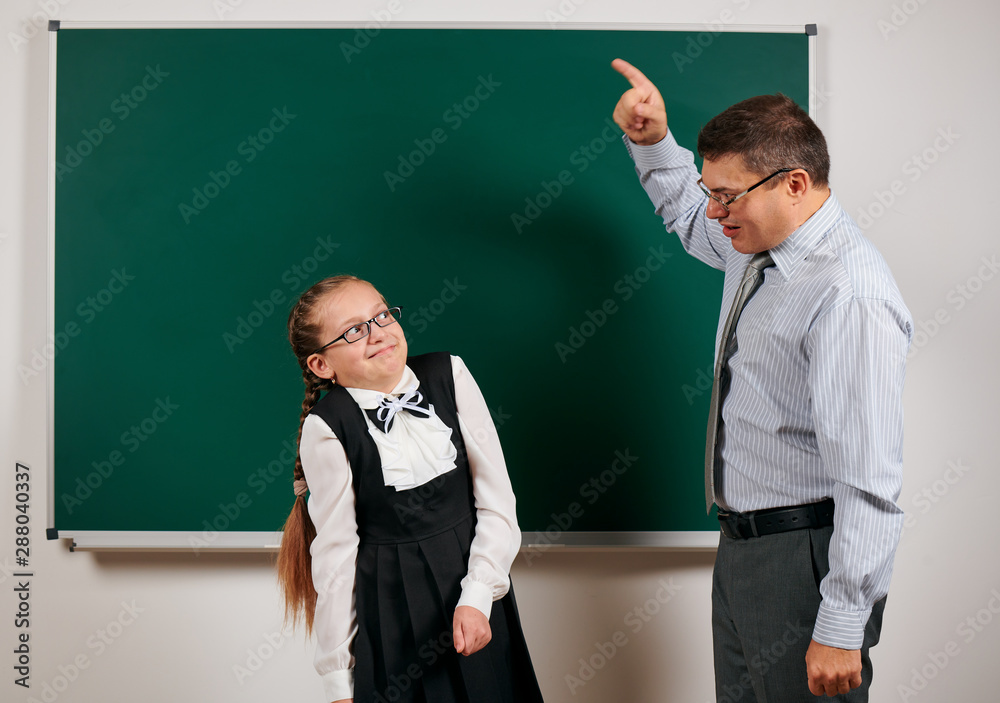 angry teacher shout to schoolgirl, posing at blackboard background ...