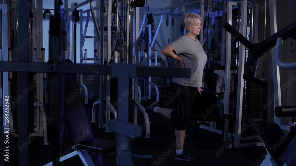 Older woman performs a standing flexion of the leg.joint gymnastics ...