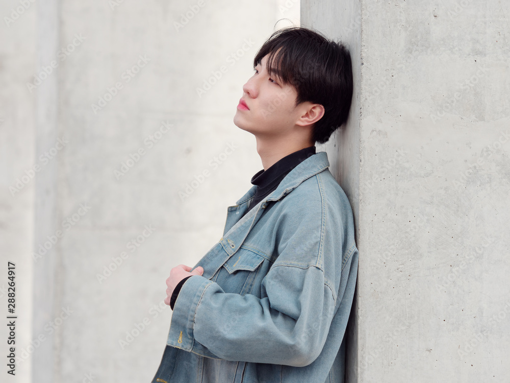 Portrait of a handsome Chinese young man in jean leaning against wall ...