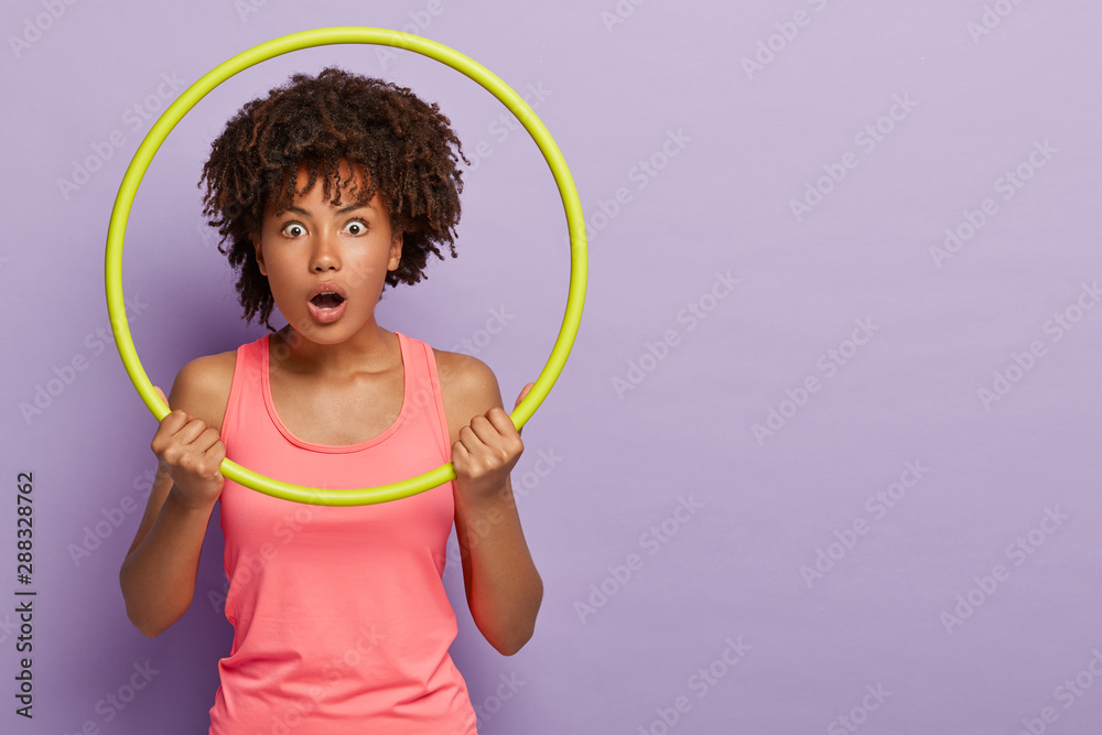 Fotografia do Stock: Stupefied fitness girl with curly hairstyle, looks ...