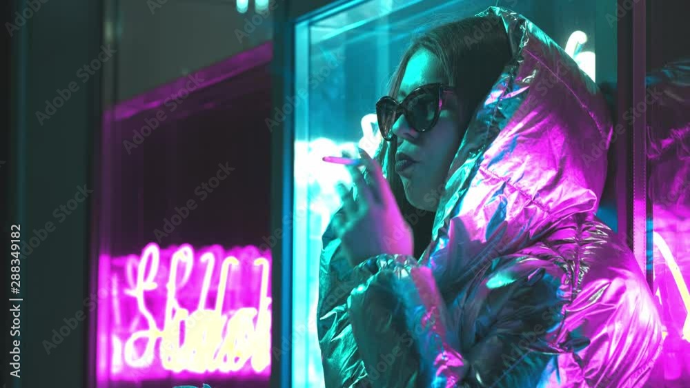 Millennial cool modern pretty girl smoking cigarette near glowing neon ...