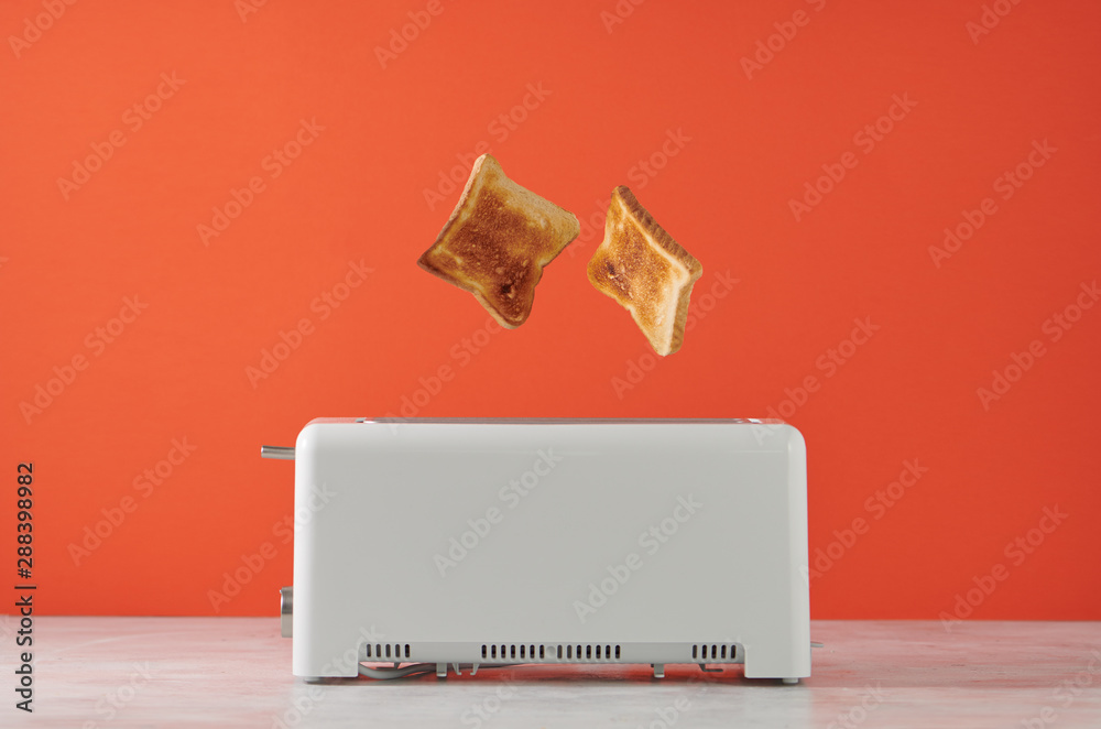 Roasted toast bread popping up of toaster with red wall, front view ...