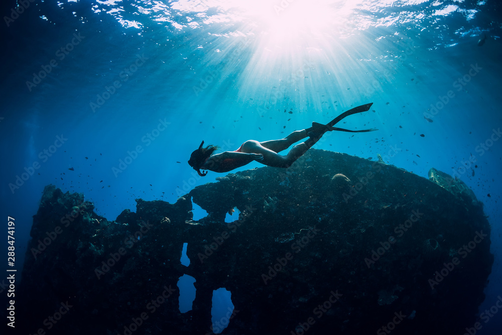 Freediver girl in pink swimwear with fins swimming underwater at wreck ...