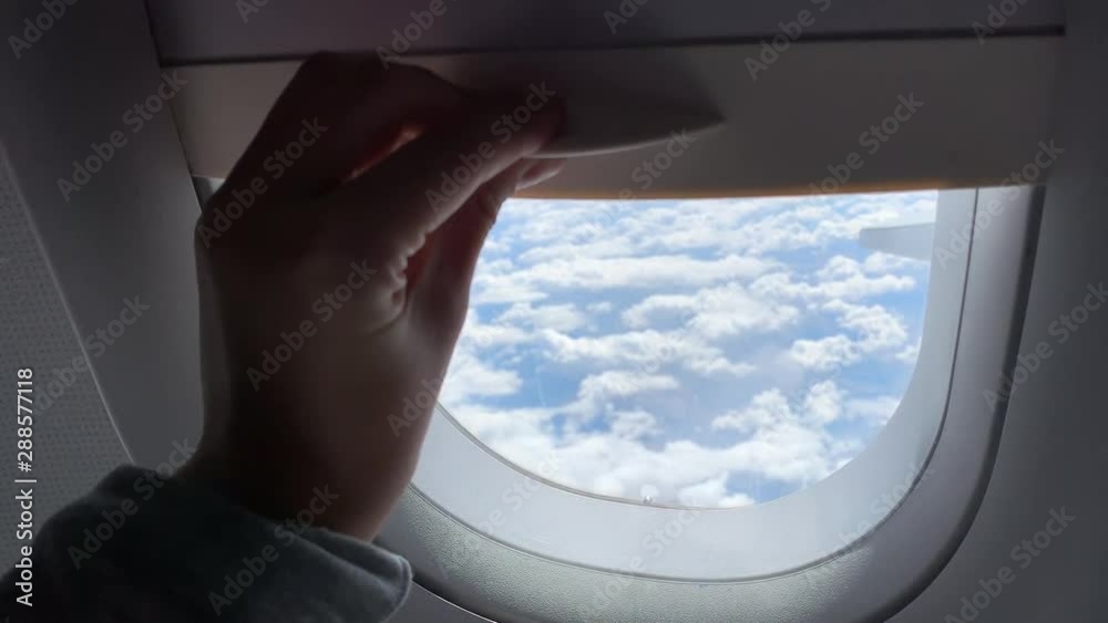 woman hand is opening window of airplane. Clouds and sky as seen ...