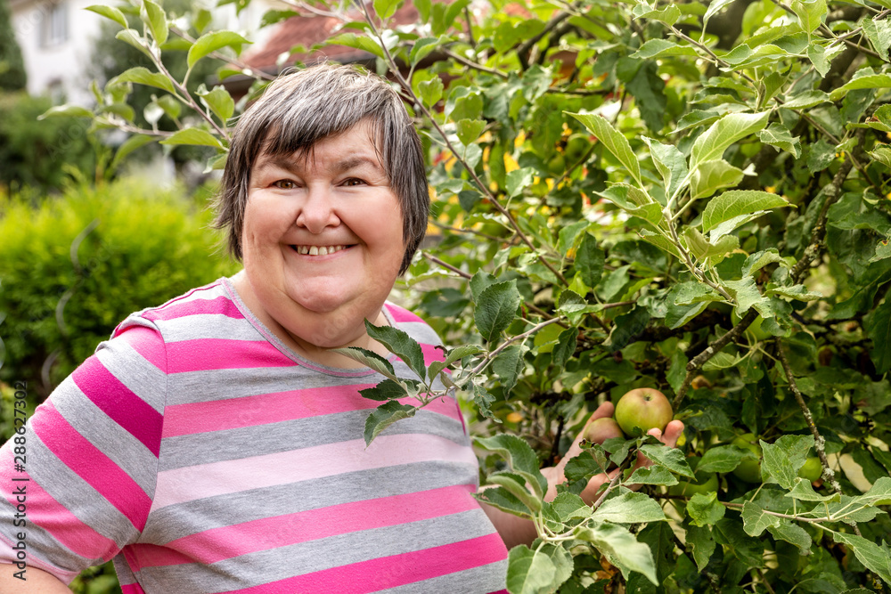 Geistig behinderte Frau steht an einem Apfelbaum, palliative Therapie ...