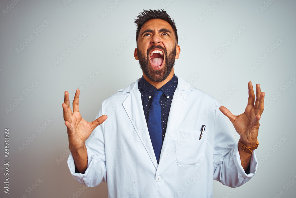 Young indian doctor man standing over isolated white background crazy ...