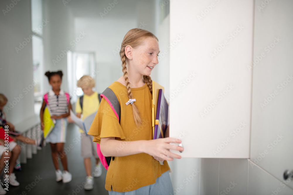 Smiling girl wearing backpack opening her locker at school Stock Photo ...