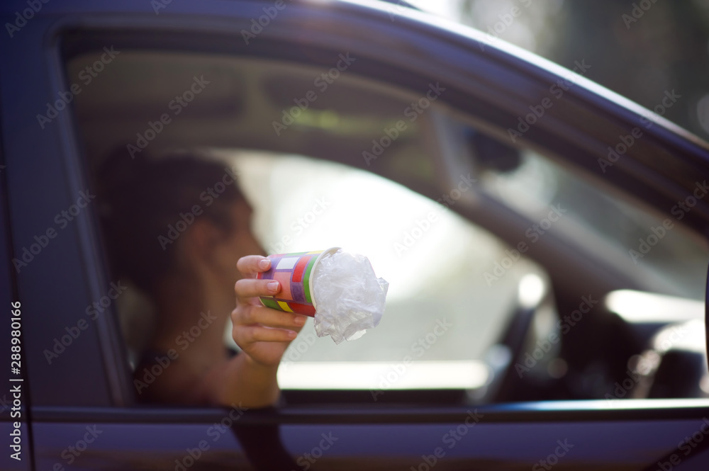 Girl holds trash outside the car window. A woman is about to throw ...