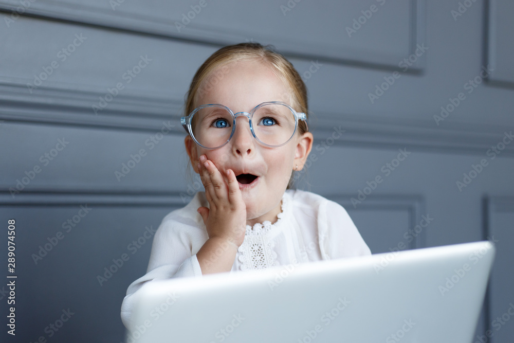 Portrait of little girl in eyeglasses behind laptop computer, making ...