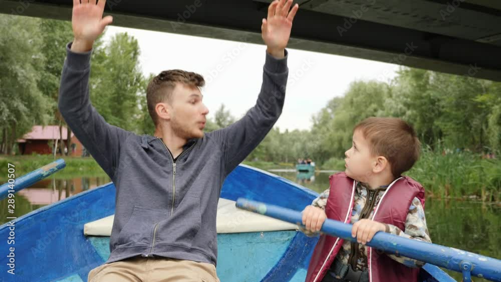 Young happy father and his little cute son floating on wooden boat ...