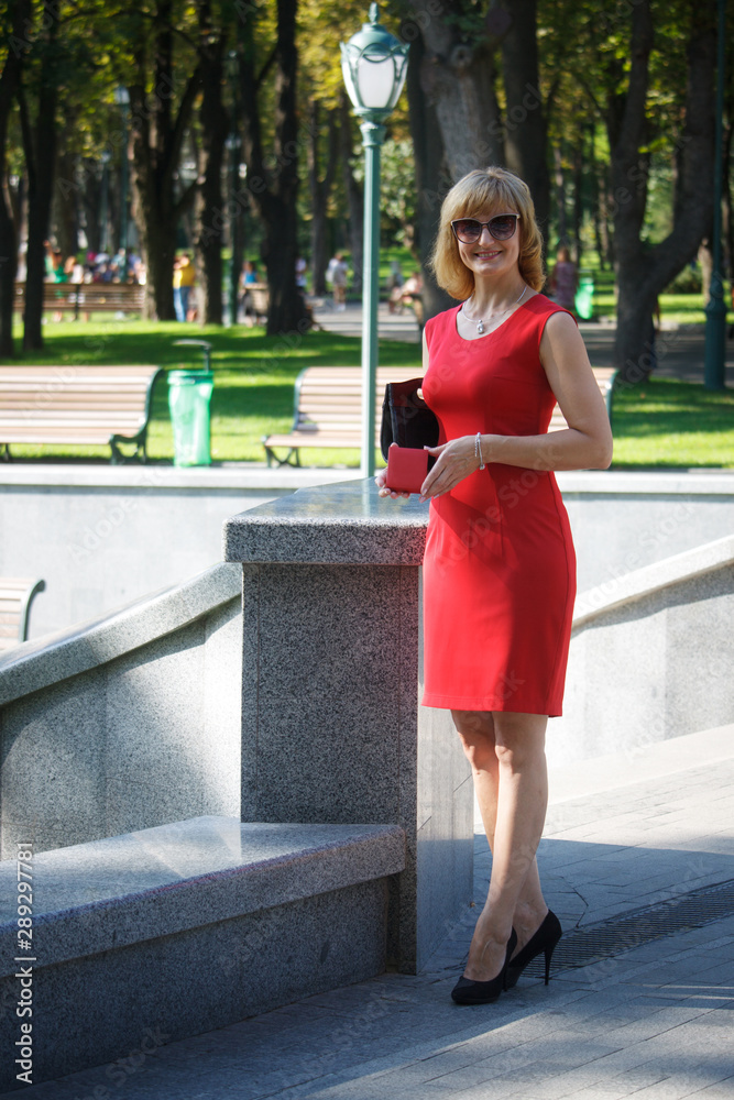 Mature middle-aged woman in red dress with a red gift box standing ...