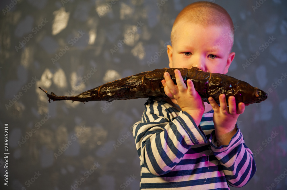 Little blond boy shows big smoked fish. Child wants to catch big fish ...