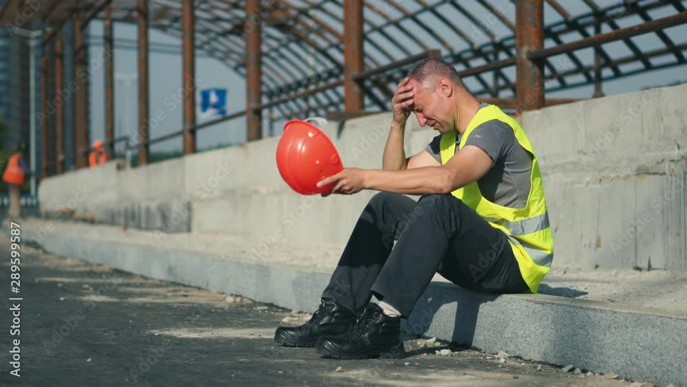 A tired worker at a construction site is upset after hard work and is ...