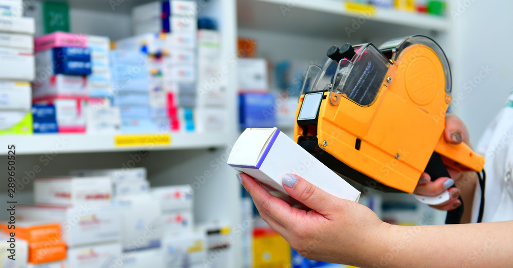 Hand of the pharmacist using yellow labeling gun for sticking price ...