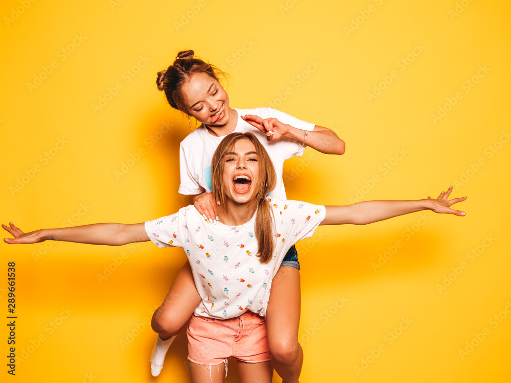 Two young beautiful smiling hipster girls in trendy summer clothes ...