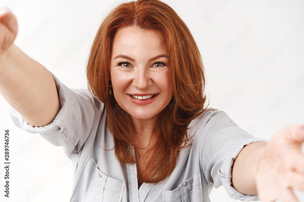 Joyful successful stylish redhead middle-aged beautiful woman taking selfie hold camera both ...