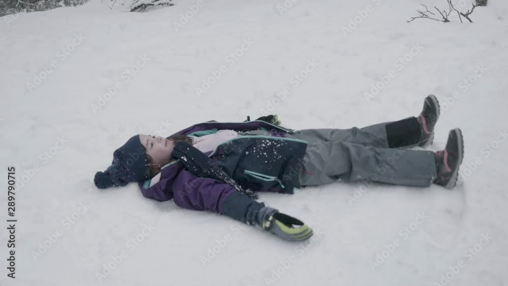 a young girl makes a snow angel by lying on her back in the snow and ...