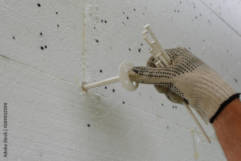 Worker gloved hand holding putting on facade white plastic screw anchor ...