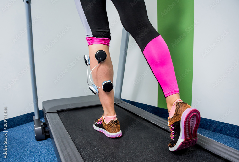 Young sports woman with electrostimulator on the muscles of the legs ...