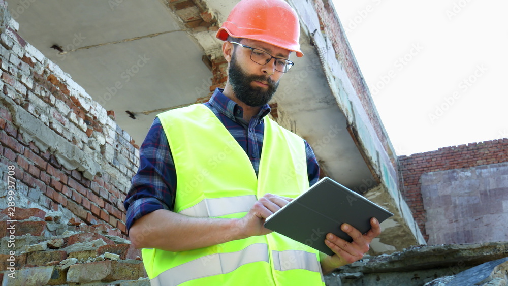 An engineer builder in a helmet use tablet, building demolition plan ...