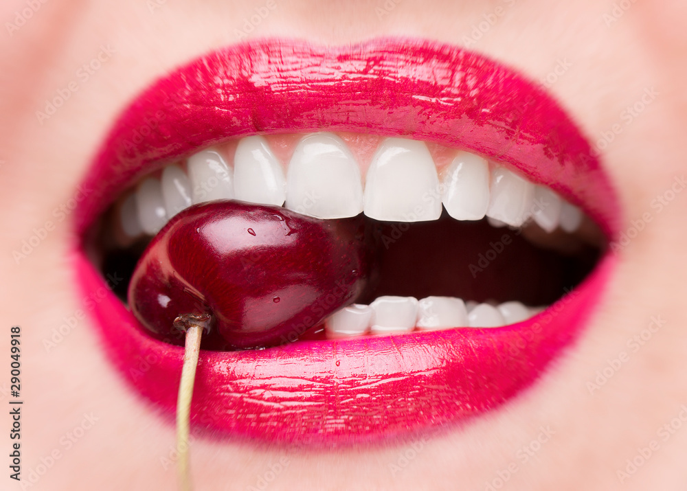 The girl bites a ripe cherry. Cherry in mouth close up. Red lipstick on ...