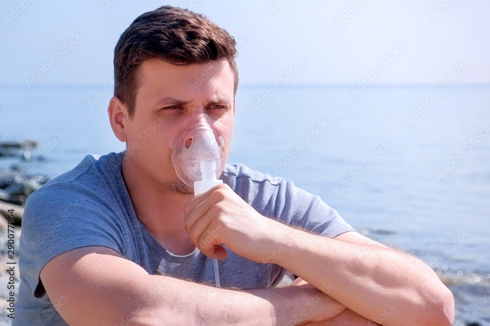 Portrait sick man uses nebulizer on seaside. Inhaling inhaler mask ...