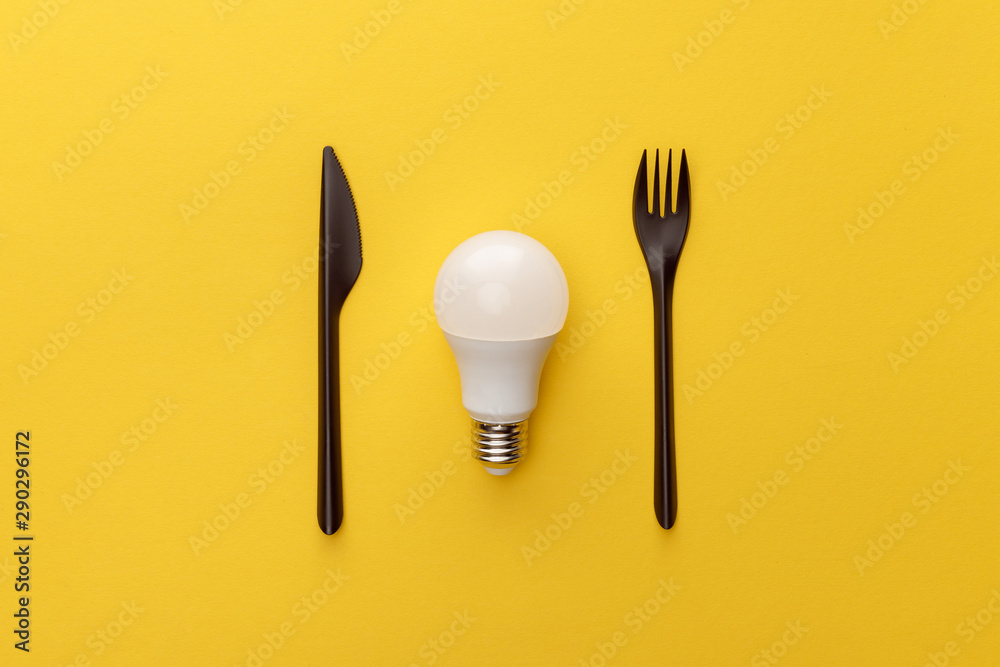 top view of light bulb between knife and fork on yellow background ...